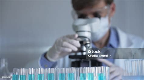 실험실 튜브에 초점이 맞춰져 있고 클로즈업 뷰입니다 흰색 보호 장갑을 낀 남자 과학자 연구원이 배경에서 현미경을 사용하고 있습니다 의학 및 과학 Stem 주제에 대한 스톡