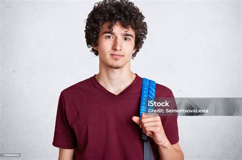 파란 배낭과 매력적인 백인 남자의 초상화 어두운 곱슬 머리를가지고 심각한 얼굴 표정으로 카메라를 직접 보고 흰색 스튜디오 배경 위에 고립 프로 모션을 위한 복사 공간 심각