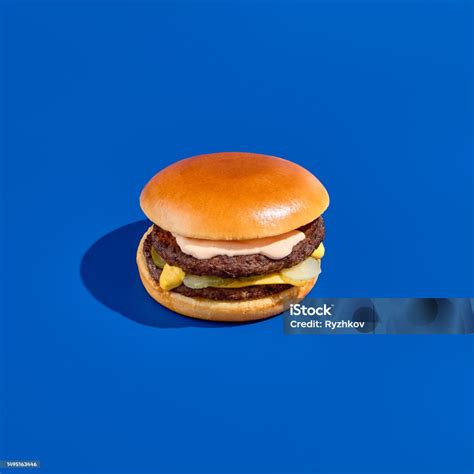 파란색 바탕에 고기가 가득한 푸짐한 더블 패티 버거 현대적인 미니멀리스트 음식 사진은 이 거부할 수 없고 관대한 패스트푸드의 풍부한 고기 맛을 강조합니다 과식에 대한 스톡
