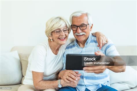 미소와 소파에 포옹 같은 태블릿을보고 노인의 부부 실내 가정 개념에서 백인 성숙하고 기술을 사용하여 은퇴 한 남자와 여자 잠금 및 검역 라이프 스타일 2명에 대한 스톡 사진