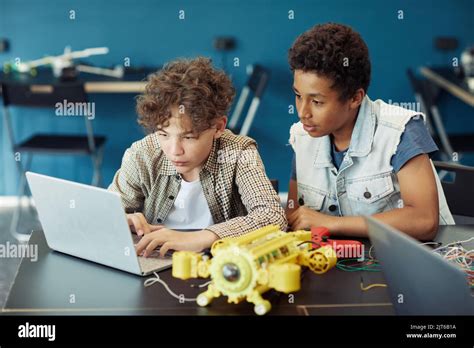 Portrait Of Two Teenage Boys Using Laptop And Programming Robot During