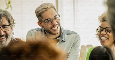 함께 즐거운 시간을 보내는 행복한 젊은 친구들의 다양한 그룹 웃고 있는 혼혈 다민족 사람들이 집에서 이야기하는 안경을 쓴 젊은이에게 집중 사진 Unsplash의