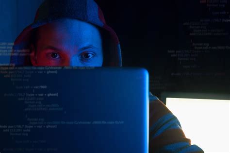 anonymous programmer hacker in hoodie coding on laptop in dark room in