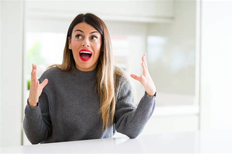 집에서 겨울 스웨터를 입고 젊은 아름다운 여자는 미친 미친 소리와 공격적인 표정과 팔을 제기 고함 좌절 개념입니다 갈색 머리에 대한 스톡 사진 및 기타 이미지 Istock