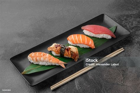 호랑이 새우 토마고 연어 참치 및 녹색 대나무 잎을 짙은 회색 질감의 배경에 젓가락이있는 검은 세라믹 접시에 넣은 니기리 세트
