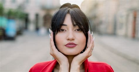 검은 머리와 패션 메이크업을 한 예쁜 갈색 머리 아시아 여성 모델의 클로즈업 얼굴 야외 초상화 손바닥에 얼굴을 기대고 오래된 도시 거리 배경에서 카메라에 포즈를 취하고