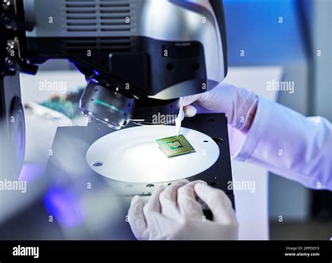 Hands Of Technician Examining Electrical Chip Under Microscope At E
