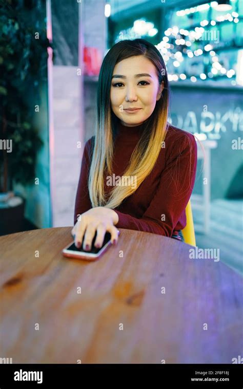 Young Asian Woman At Table In Cafe Holds Hand On Mobile Phone
