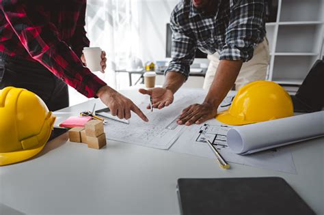 엔지니어는 건축 계획에 대한 청사진을 가지고 팀으로 작업합니다 건축가 장비로 건설 프로젝트 개념을 스케치하는 엔지니어 테이블에서 이야기하는 건축가 팀워크와 건설 개념 2명에