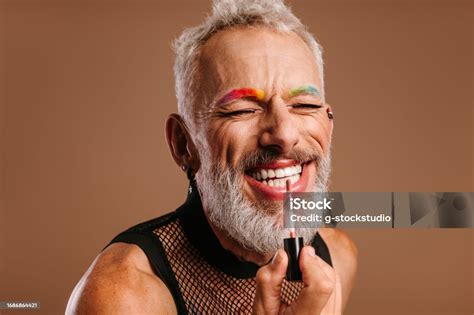 Happy Mature Gay Man With Sincere Smile Applying Makeup Against Brown