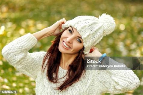 화이트 니트 Sweather 및 모자에 화려한 웃는 여자가을 공원 그리고 카메라에 포즈에 낙된 엽과 녹색 잔디에 앉아 가을에 대한 스톡 사진 및 기타 이미지 Istock
