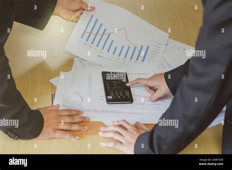 Two Colleagues Discussing Stock Graph Data With Smart Phone And New Modern Computer Laptop On