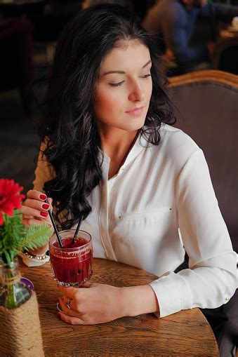 여자는 커피 숍에서 멀드 와인을 마신다 흰색 셔츠와 레스토랑 카페에서 알코올 레드 와인 한 잔을 들고 손톱에 적갈색 바니시에 세련된 소녀 곱슬 머리에 대한 스톡 사진 및