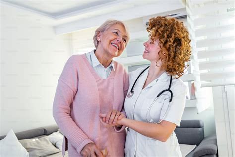 웃는 간호사가 노인 여성이 요양원을 돌아다니는 것을 돕고 있습니다 행복한 여성 간병인과 집에서 함께 걷는 노인 여성의 초상화 노인 여성을 돌보는 전문 간병인 사진