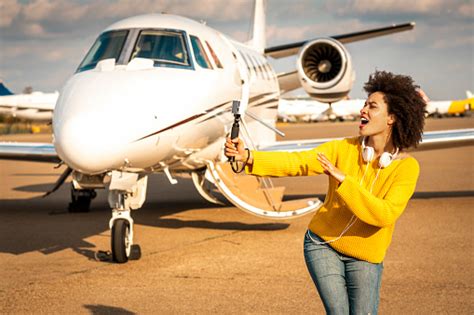 젊은 여성 동영상 블로거는 자신을 촬영 그녀의 카메라로 셀 카 스틱에 장착 된 공항 활주로에 주차 된 개인 비행기 옆에 Monopod에 대한 스톡 사진 및 기타 이미지