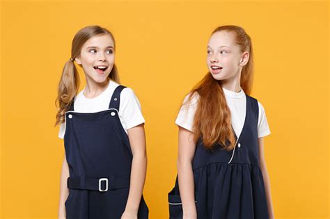 노란색 배경 어린이 스튜디오 초상화 어린 시절 어린이 교육 라이프 스타일 개념 모의 복사 공간에 고립 된 흰색 티셔츠 블루 학교 유니폼 드레스를 입은 두 명의 어린 소녀