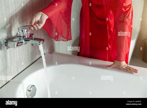 A Woman In Red Silk Nightgown Turns On The Faucet At The Bathtub Women