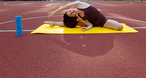 검은 양복을 입은 젊은 운동 여성이 경기장 한가운데있는 노란색 매트 위에서 스트레칭을하고 있습니다 한 여성이 도시에서 훈련하고 있습니다 초상 20 24세에 대한 스톡 사진