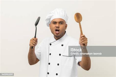 유니폼을 입은 젊은 잘 생긴 아시아 남자 요리사는 터너와 래들 용품을 들고 부엌에서 요리하는 고립 된 배경에서 다양한 제스처