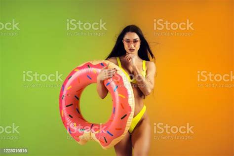 그라데이션 배경에 세련된 노란색 수영복에 고무 도넛과 젊은 적합과 스포티 한 여성의 패션 초상화 여름을 위한 완벽한 바디 계절에 대한 스톡 사진 및 기타 이미지 Istock