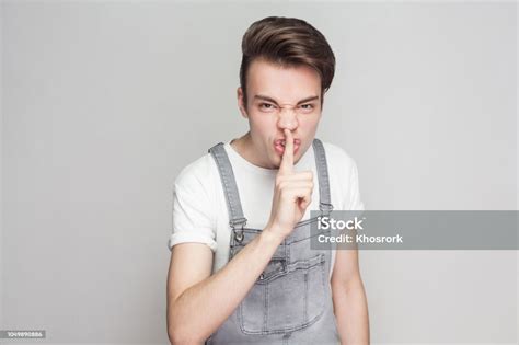 서 카메라를 보고 하 고 조용한 기호를 보여주는 흰색 T셔츠와 데님 바지와 캐주얼 스타일에 성 난 젊은 갈색 머리 남자의 초상화 20 29세에 대한 스톡 사진 및 기타