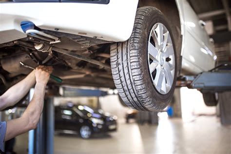 자동차 주유소에서 리프트수리를 위해 차량이 들어 올려져 있으며 그 중에는 바지 수리를 하는 정비사가 있습니다 휠 클로즈업 타이어 서비스 건강 진단에 대한 스톡 사진 및 기타