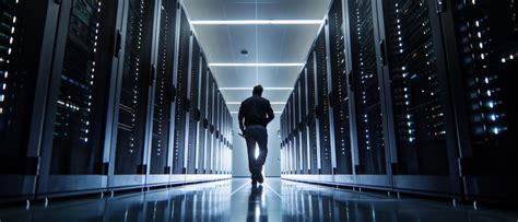 an it technician walks through rows of server racks in a data center while simultaneously