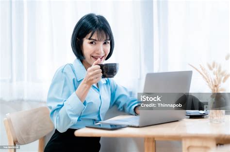 치과 교정기로 미소 짓는 아시아 프리랜서 사업가들은 커피숍에서 노트북과 스마트폰이 있는 노트북 컴퓨터와 함께 일하는 커피잔 머그잔을 들고 캐주얼하게 일한다 25 29세에