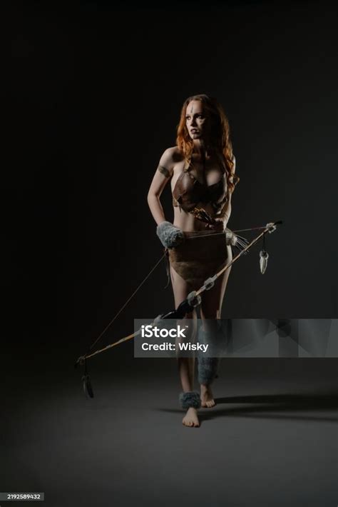 Woman Dressed In Primitive Attire Poses With A Handmade Bow In A Dim