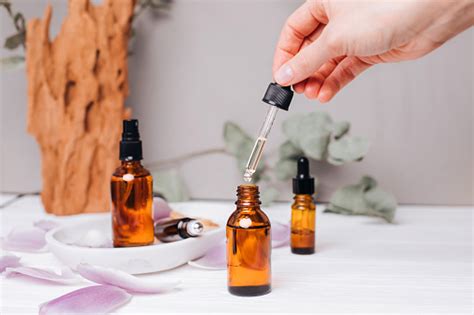 여성의 손은 얼굴 화장품이 든 피펫 나무 테이블에 유칼립투스 가지가 있는 쟁반에 액체가 든 호박색 병 페이셜 클리너 세럼을 들고 있습니다 갈색에 대한 스톡 사진 및 기타