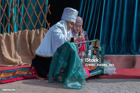 노령자 여성과 전국 카자흐 의상을 입은 어린 소녀가 거리 극장 공연 중 리본으로 전통적인 베식 침대를 장식합니다 카자흐스탄에 대한 스톡 사진 및 기타 이미지 Istock