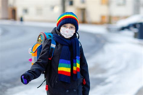 학교에 가는 길에 의료 용 마스크를 쓰고 안경을 쓴 어린 아이 소년 어린이 배낭 가방 따뜻한 옷을 입고 겨울 날 에 학교 키드 코로나 전염병 중 잠금 및 검역 시간 겨울에