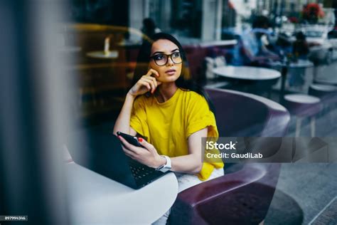 작품에 구현에 대 한 창의적인 아이디어에 대해 생각 하 고 멀리 보고 유행 안경에 명상 매력적인 그래픽 디자이너 화려한 갈색 머리 학생 커피숍에 앉아있는 동안 숙고 Cd