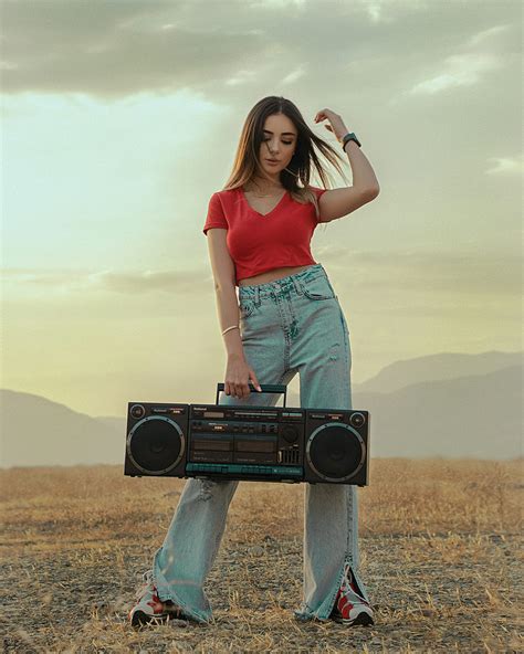 빨간 셔츠와 파란색 데님 청바지를 입은 여자가 검은 스피커를 들고 있다 사진 Unsplash의 무료 테헤란 이미지