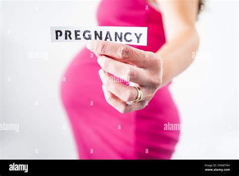 Pregnant Woman Holding Pregnancy Sign Towards The Camera Wearing Pink Dress In The Ninth Month