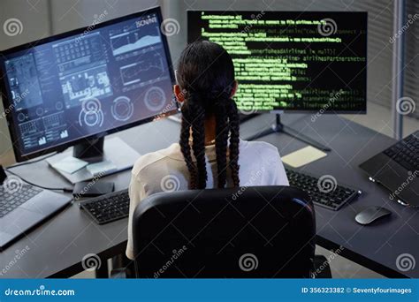back view of female it developer coding on multiple computers at workstation in office stock