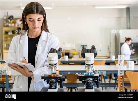 Female Scientist Examining Liquid On Microscope With Colleague Working At Laboratory Stock Photo