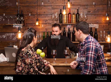 Couple Talking To Bartender Behind Bar Counter In A Cafe Hipster