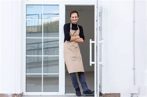 앞치마를 입고 카페의 바 카운터에 기대어 얼굴 털을 가진 미소 짓는 젊은 남자의 초상화 텍스트 또는 이미지에 대한 빈 슬레이트 보드 복사 공간입니다 바텐더 오너 스태프