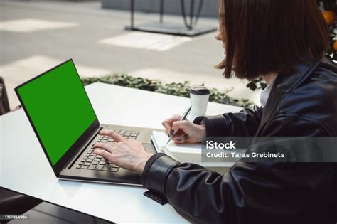 여성 프리랜서 카피라이터 메모장에 텍스트를 쓰고 모니터에 녹색 화면 크로마 키가 있는 랩톱 컴퓨터의 키보드를 입력하는 측면