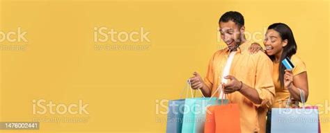 신용 카드를 들고 노란 스튜디오 배경에 밝은 쇼핑백 안을 들여다보는 흥분된 젊은 아프리카계 미국인 커플 남자에 대한 스톡 사진 및 기타 이미지 Istock