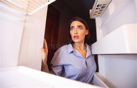 Shocked Girl Looking At Her Empty Fridge Shelves In Despair Stock Image