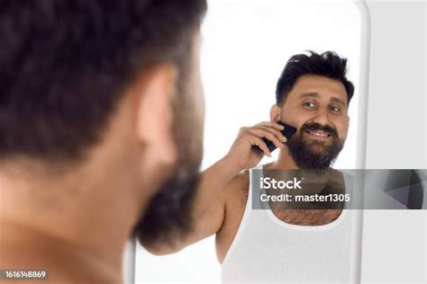 거울을 보며 웃고 있는 성숙한 남자 수염을 돌보고 하얀 스튜디오 배경에 면도기로 면도한다 35 39세에 대한 스톡 사진 및 기타 이미지 Istock