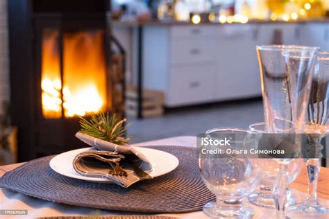 크리스마스와 새해를 위해 장식 된 로프트 하우스 내부의 스토브 벽난로 근처에서 접시 포크 나이프 냅킨 안경이있는 축제 테이블을 제공합니다 축제 저녁 식사를 위해 손님을