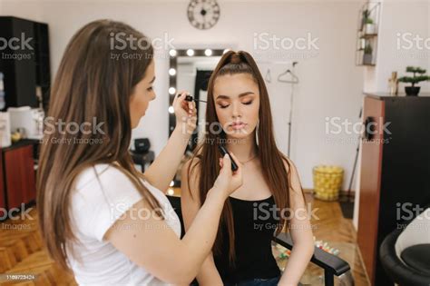큰 거울 앞에 앉아 있는 미용실에서 젊은 빨간 머리 소녀를 위한 메이크업을 하는 아름다운 여성 메이크업 아티스트 휴일 및 회의를