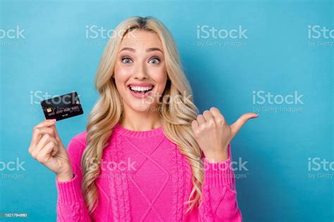 물결 모양의 머리를 한 인상적인 여성의 초상화는 분홍색 풀오버를 입고 직불 카드를 들고 파란색 배경에 고립된 빈 공간을 지시한다