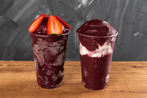 플라스틱 컵에 딸기와 연유를 넣은 브라질산 냉동 Aã§ai 베리 아이스크림 스무디 2개 나무 책상과 회색 여름 배경 메뉴 및 소셜 미디어 전면 보기 프리미엄 사진