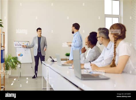 Young Man Making Business Presentation In Front Of Office Whiteboard During Team Meeting Stock