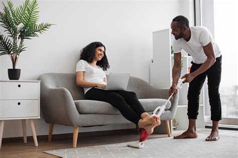 남자가 카펫을 진공 청소기로 청소하는 동안 노트북에서 일하는 웃는 여자 남자에 대한 스톡 사진 및 기타 이미지 남자 남편 진공청소기 Istock