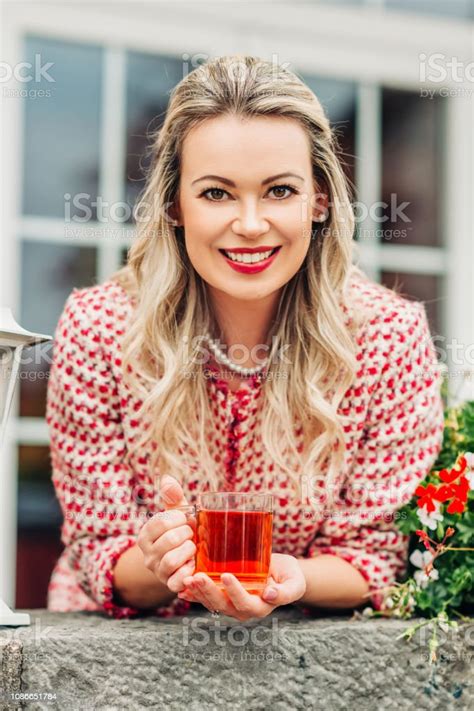 테라스에 서 서 차 잔을 들고 빨간색과 흰색 체크 무늬 재킷을 입고 금발 머리를 가진 아름 다운 여자의 레트로 스타일 초상화